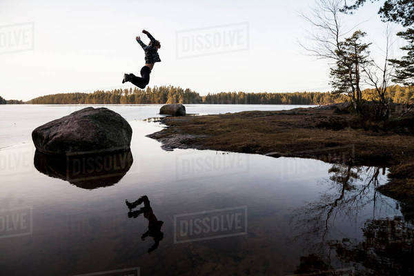 Full length of boy jumping off stone over water - Stock Photo - Dissolve