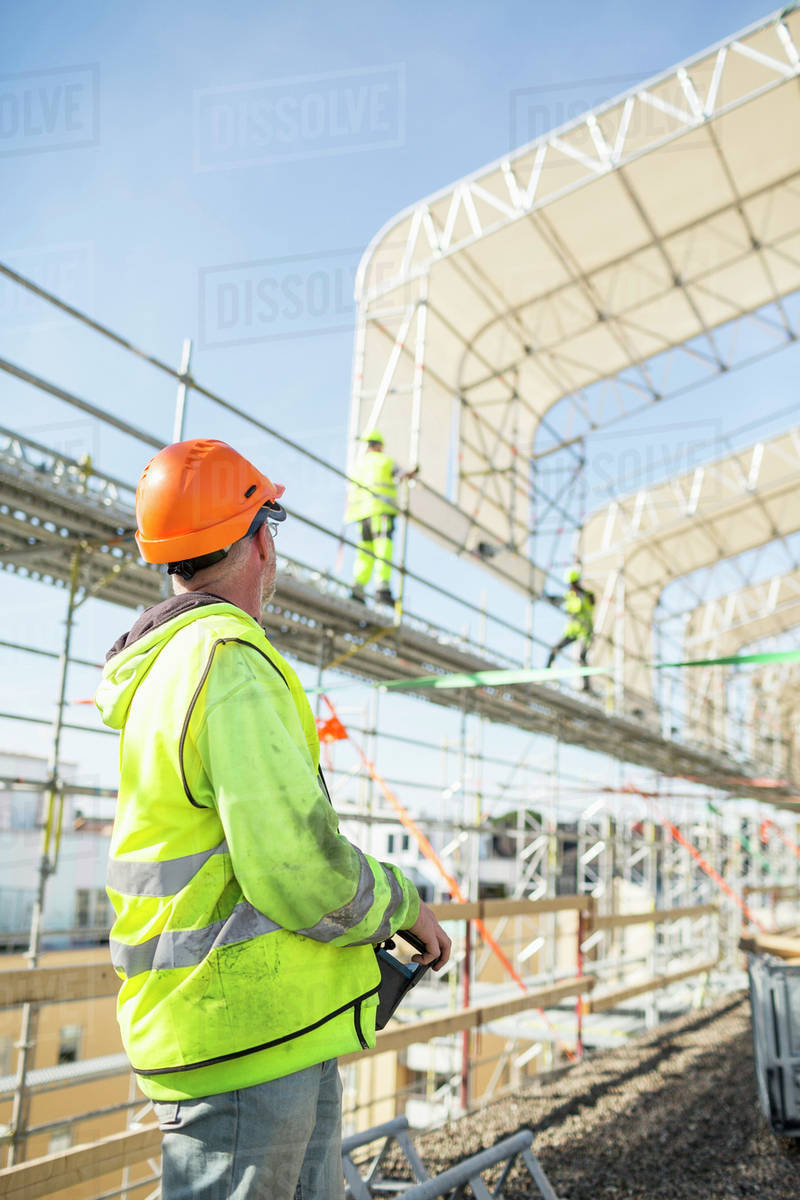 Side view of construction worker looking at colleagues working at site ...