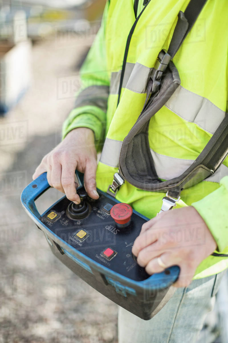 Midsection of construction worker operating control tool at site ...