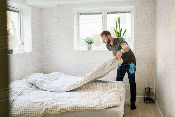 Full length of man making bed in house - Stock Photo - Dissolve