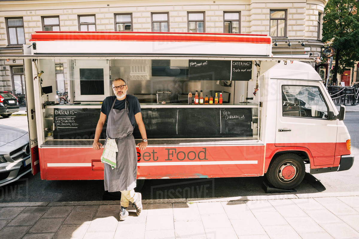 Full length of male chef standing against food truck at city street ...
