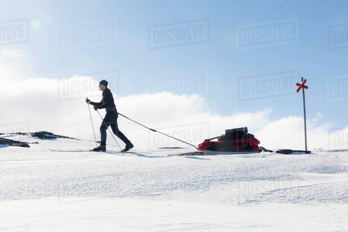 Full length side view of man pulling sled with luggage on snow covered ...