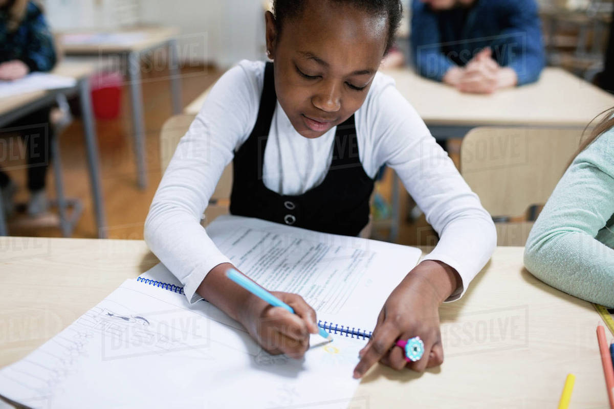Smiling girl studying at desk in classroom - Royalty-free Stock Photo ...