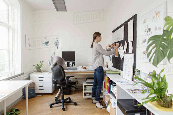 Full length of artist sticking documents on bulletin board in creative ...