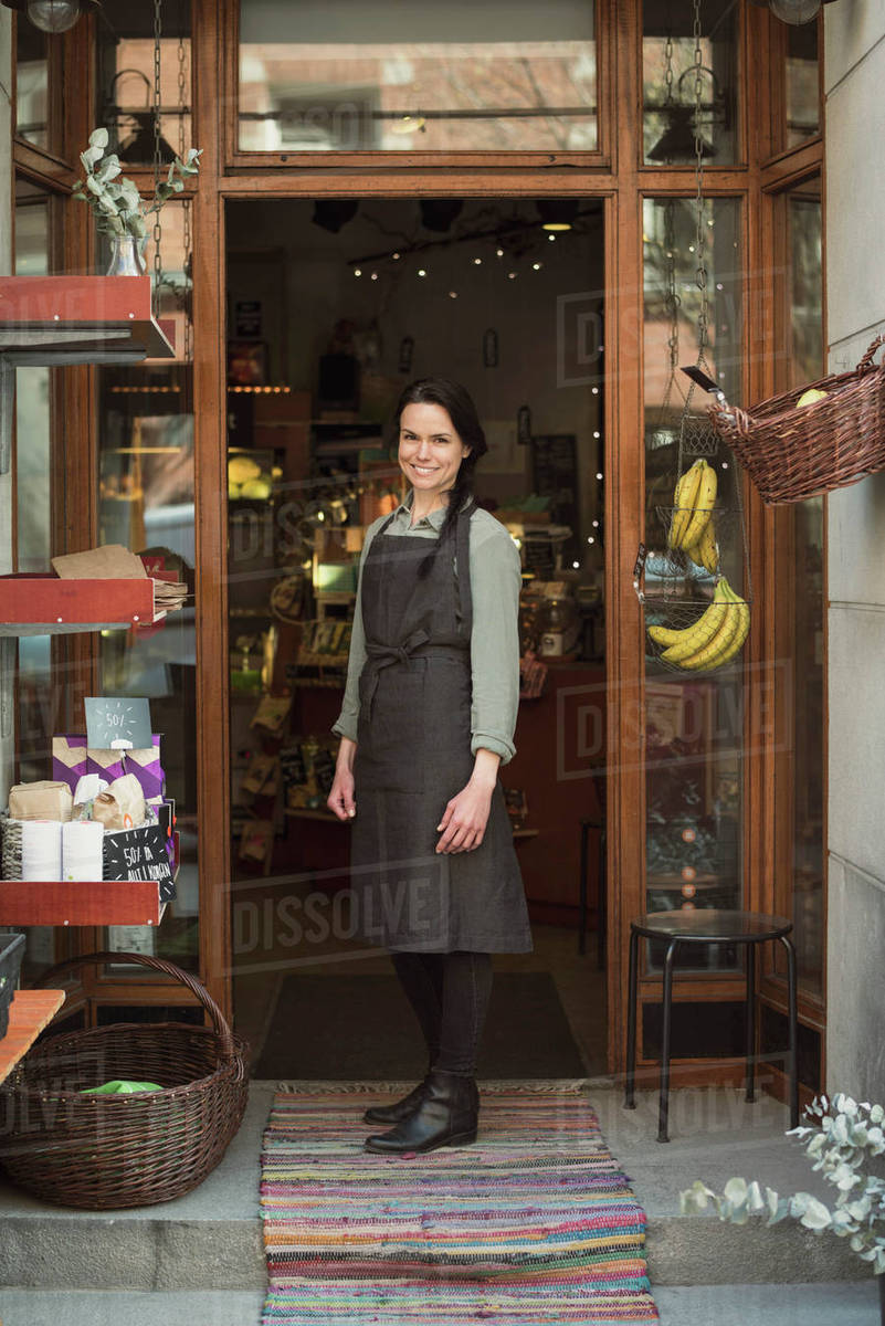Full length portrait of smiling owner standing at store entrance ...
