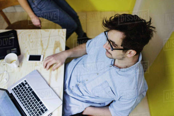 High angle view of young man sitting with laptop at desk in office ...