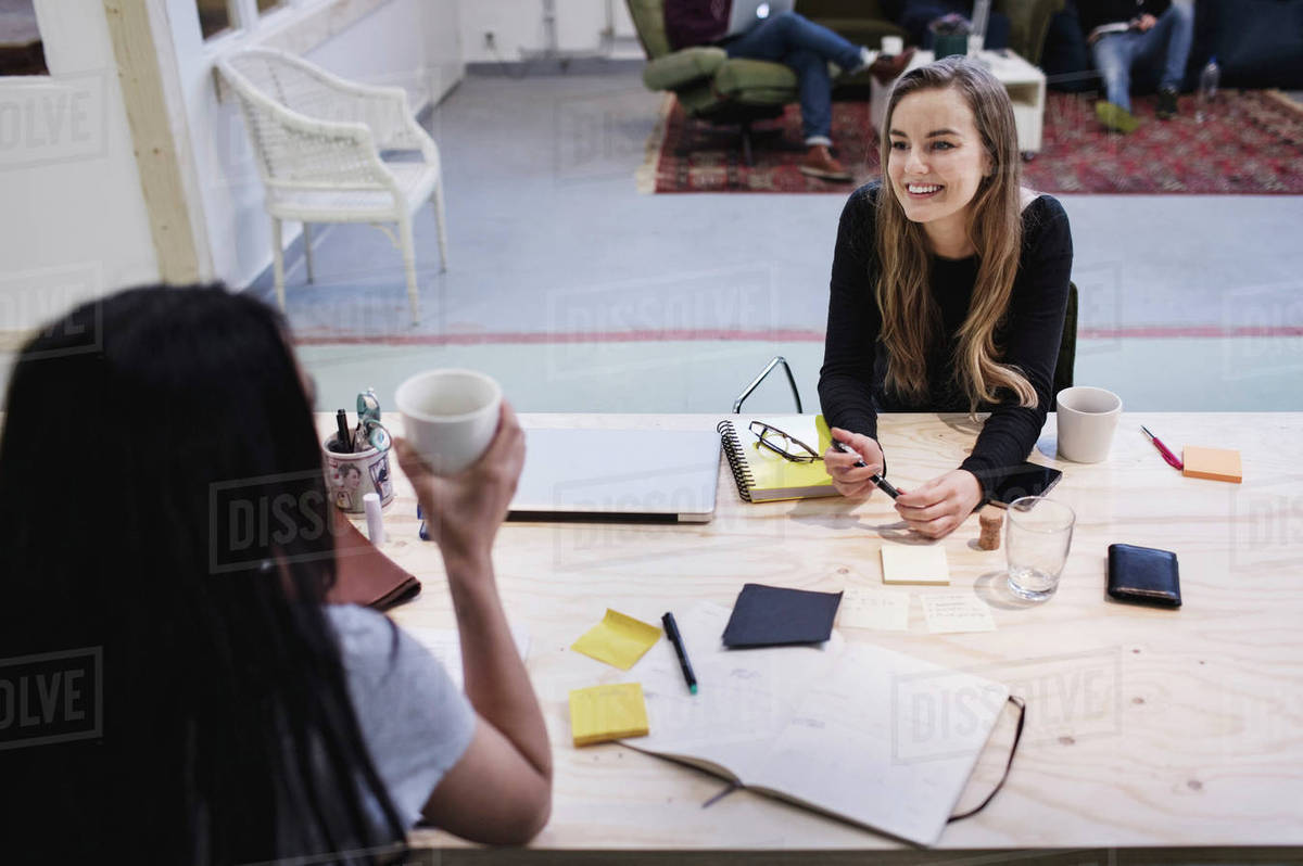 High angle view of two happy women talking to colleague at desk in ...