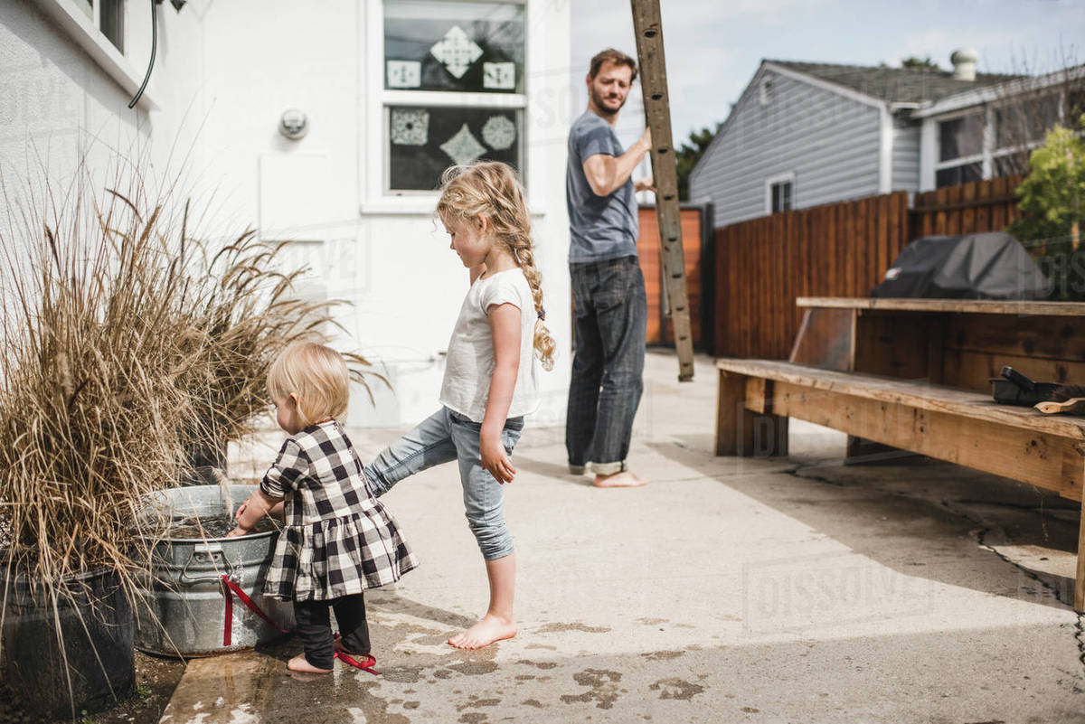 Father carrying ladder while looking at daughters playing with water ...