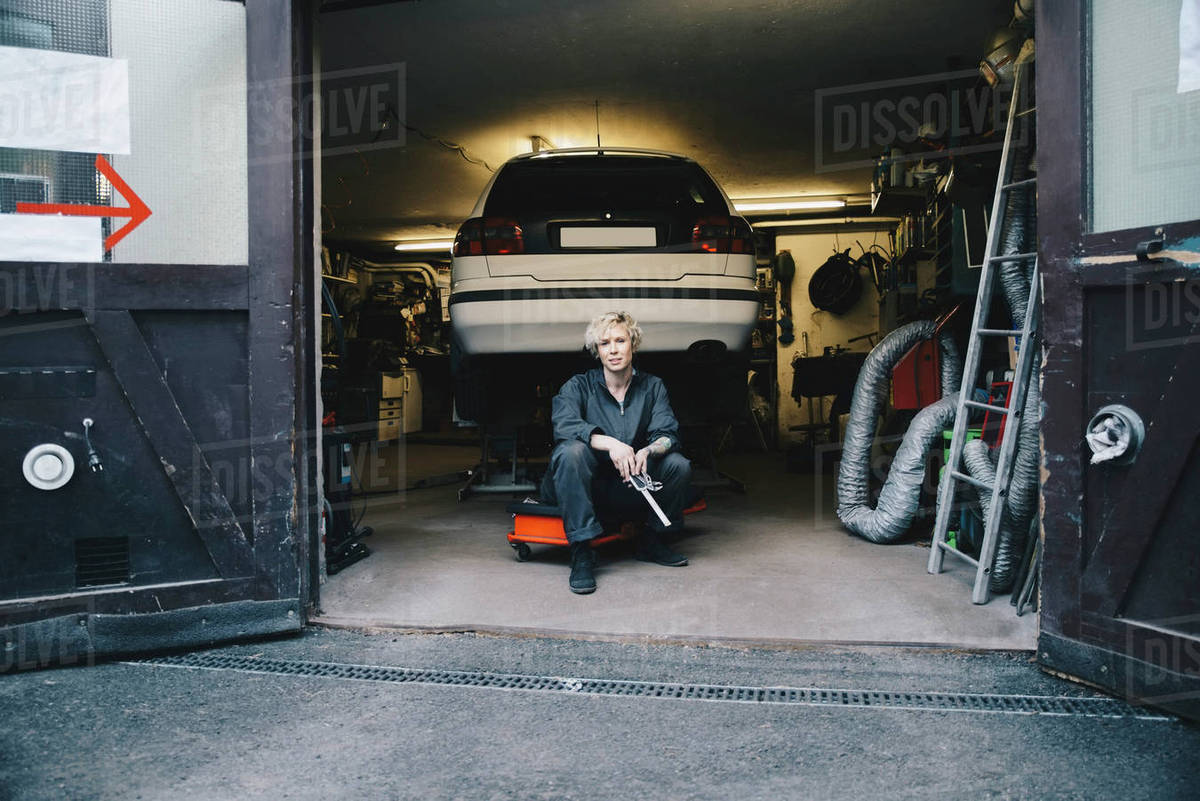 Female mechanic sitting by car at entrance of auto repair shop ...