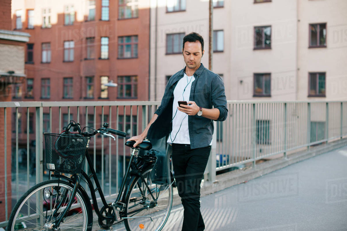 Man using mobile phone while walking with bicycle on footbridge against ...