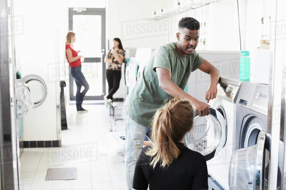 University student talking to woman by washing machine while friends ...