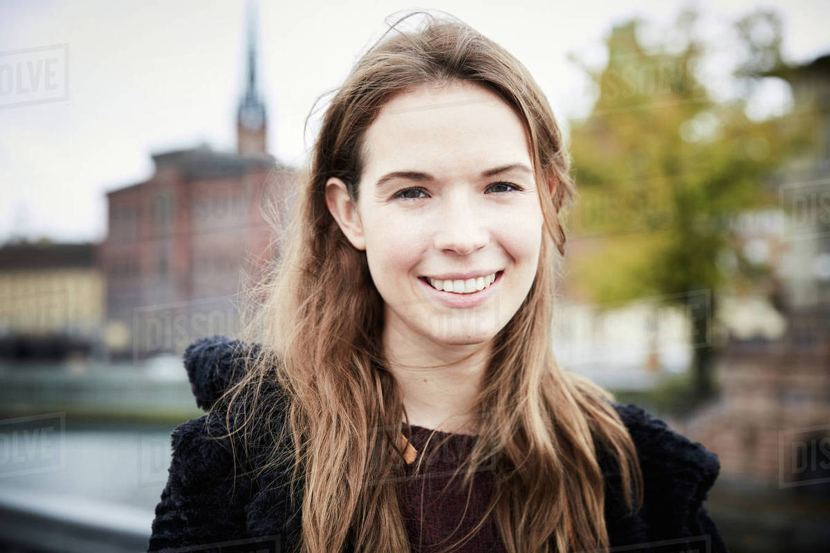 Close-up portrait of smiling young woman with brown hair in city ...