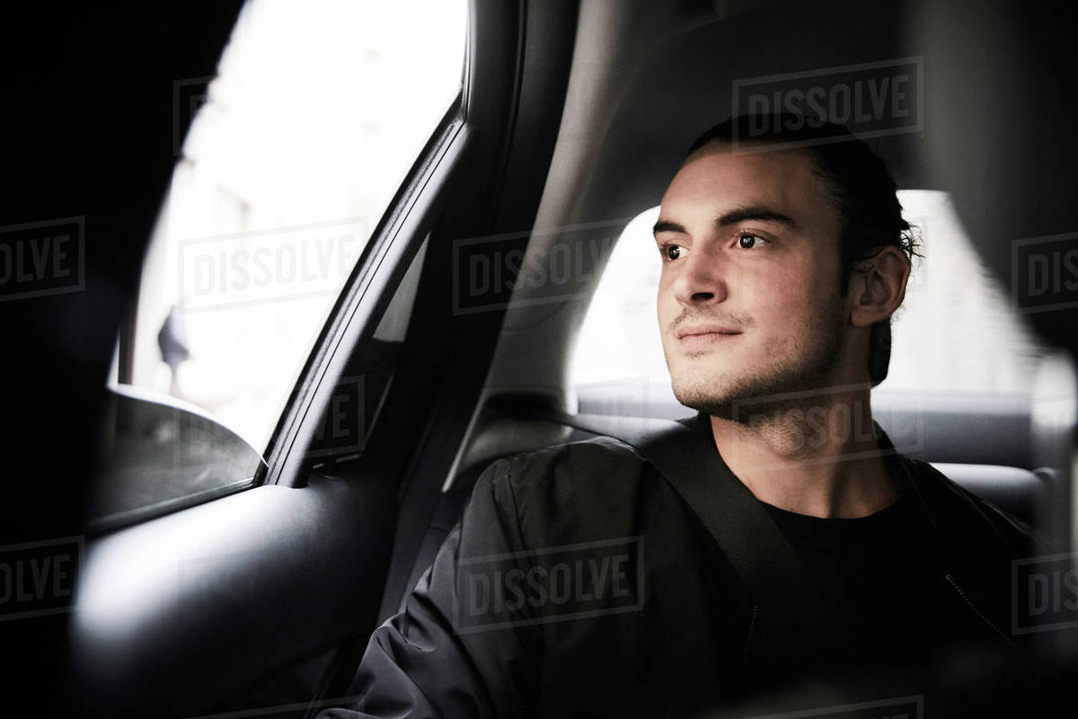 Thoughtful young man looking through window while riding in car at city ...