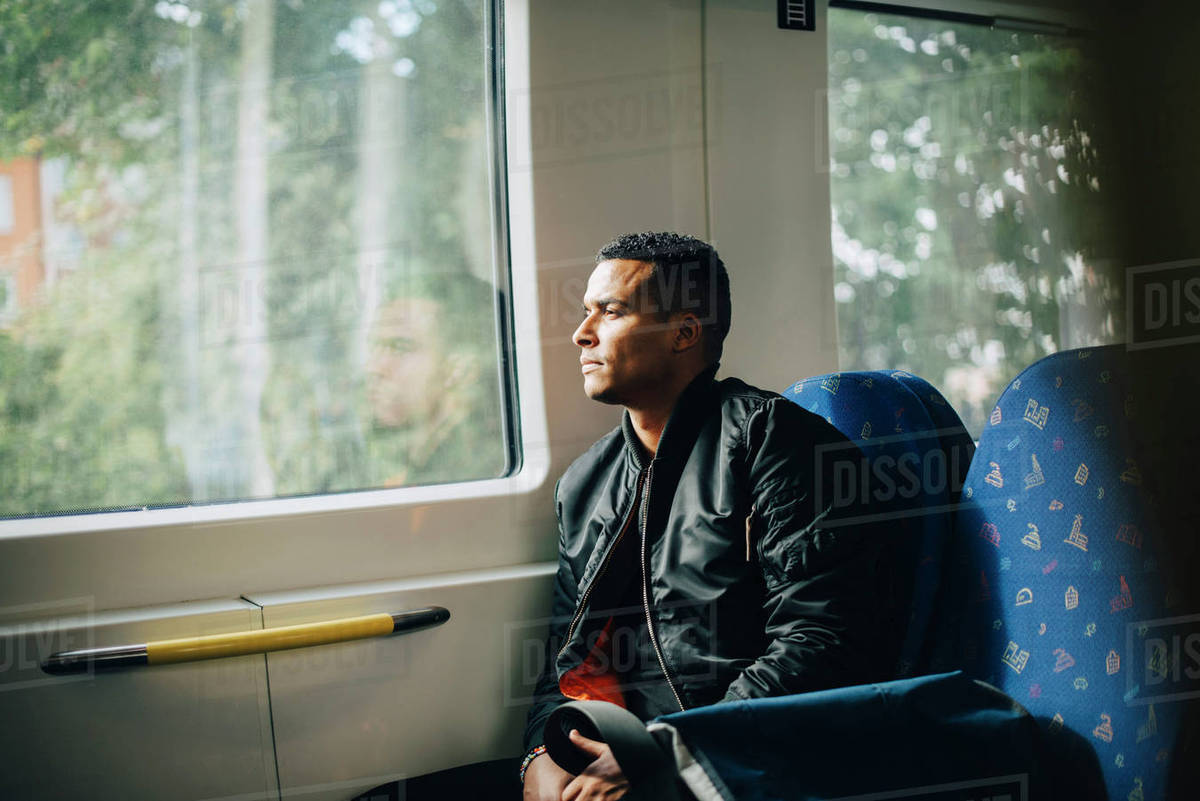 Thoughtful man looking through window while sitting in train - Stock ...