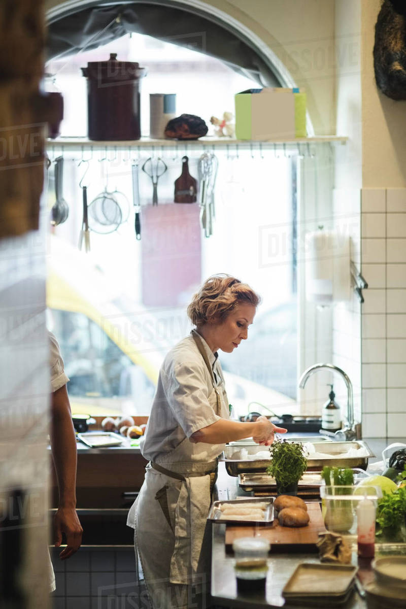 Side view of female chef preparing food on counter in kitchen at ...