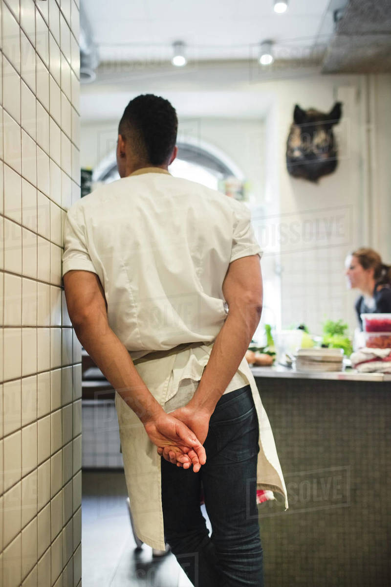 Rear view of male chef standing with hands behind back by wall in ...