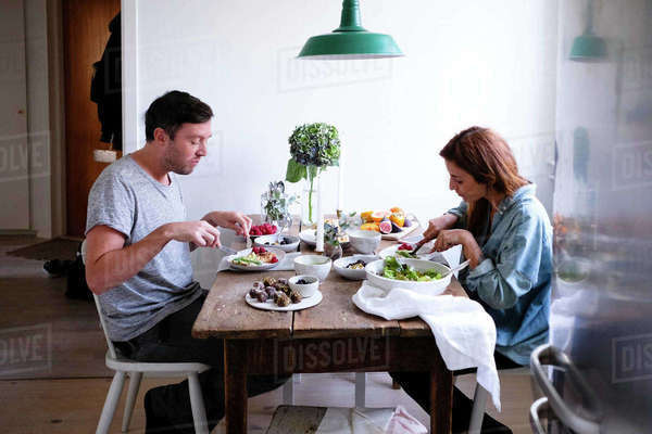 Side view of couple having food at table while sitting by wall ...