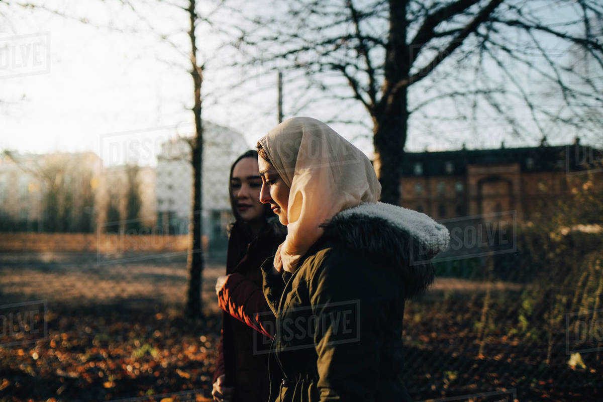 Side view of young female Muslim friends walking in city during sunset ...