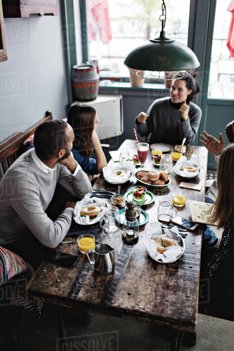 High angle view of friends talking while having food at dining table ...
