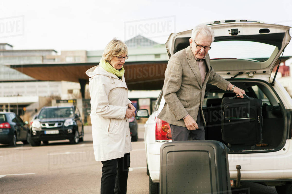 Senior man unloading luggage from car trunk by woman standing in ...