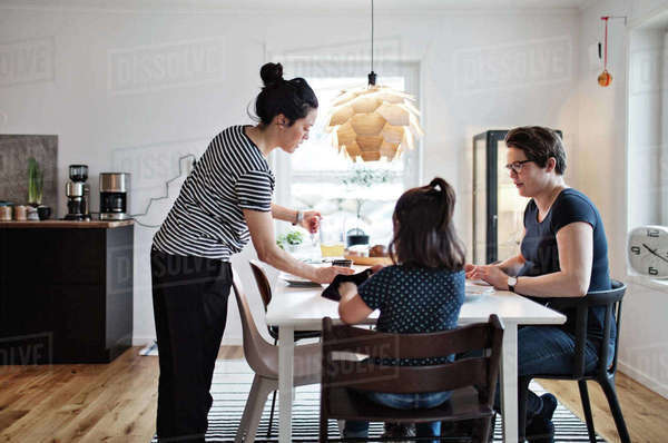 Female serving food to girl and woman at dining table - Royalty-free ...