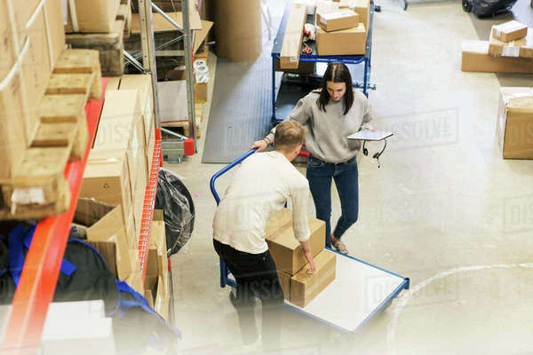 High angle view of colleagues loading boxes on push cart in industry ...