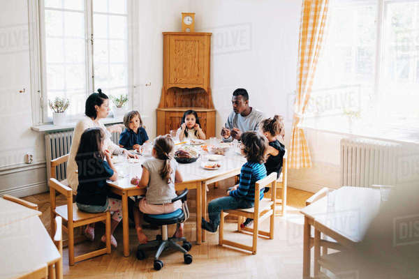 Teachers and students eating lunch at table in kindergarten classroom ...