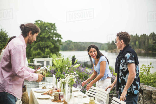 Happy multi-ethnic friends setting table for dinner party in backyard ...