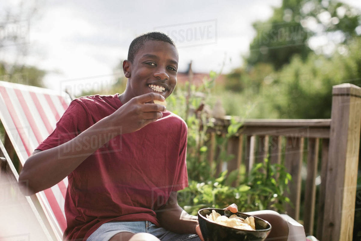 Portrait of smiling boy eating snack while sitting at porch - Royalty ...