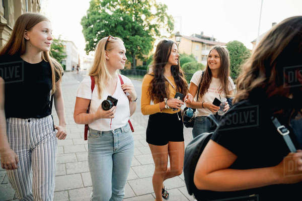 Female friends with camera and mobile phone talking while exploring ...