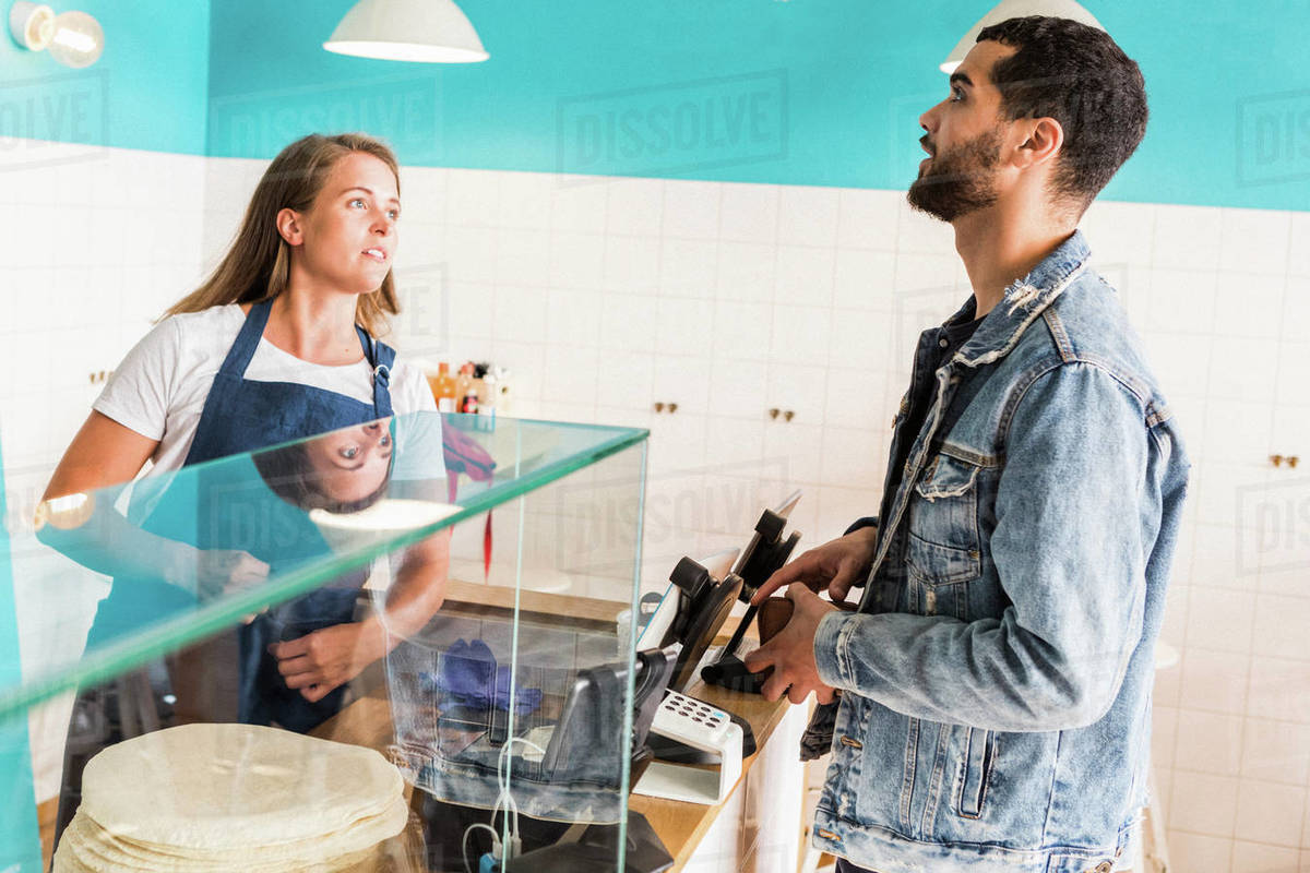 Young male customer standing with female owner at checkout in ...