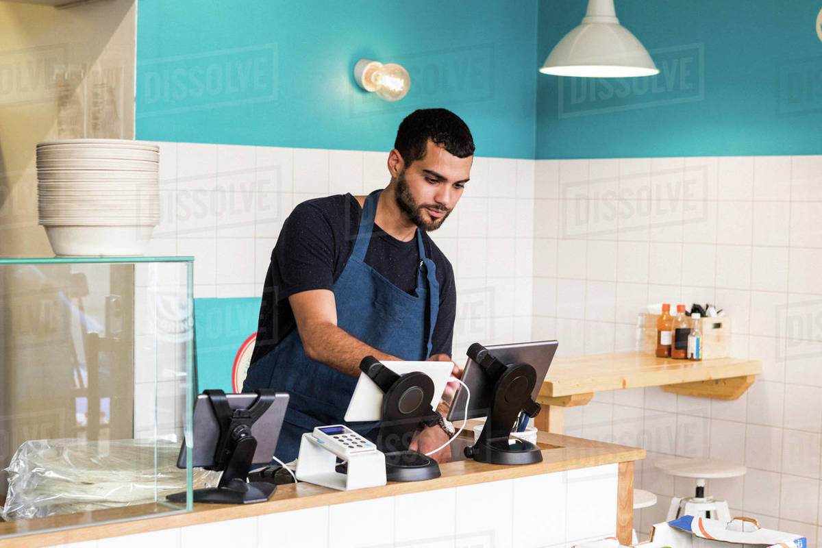 Confident young owner using digital tablet at checkout in restaurant ...