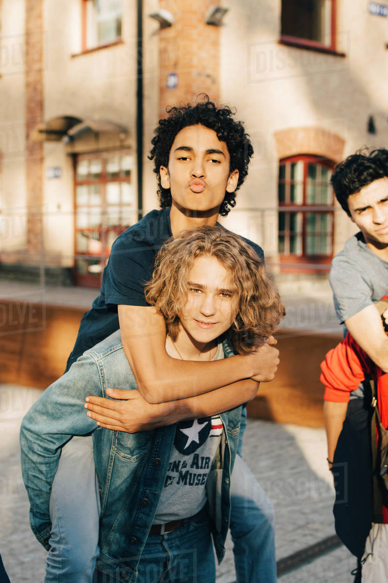 Portrait of teenage boy puckering while being piggybacked by friend in ...