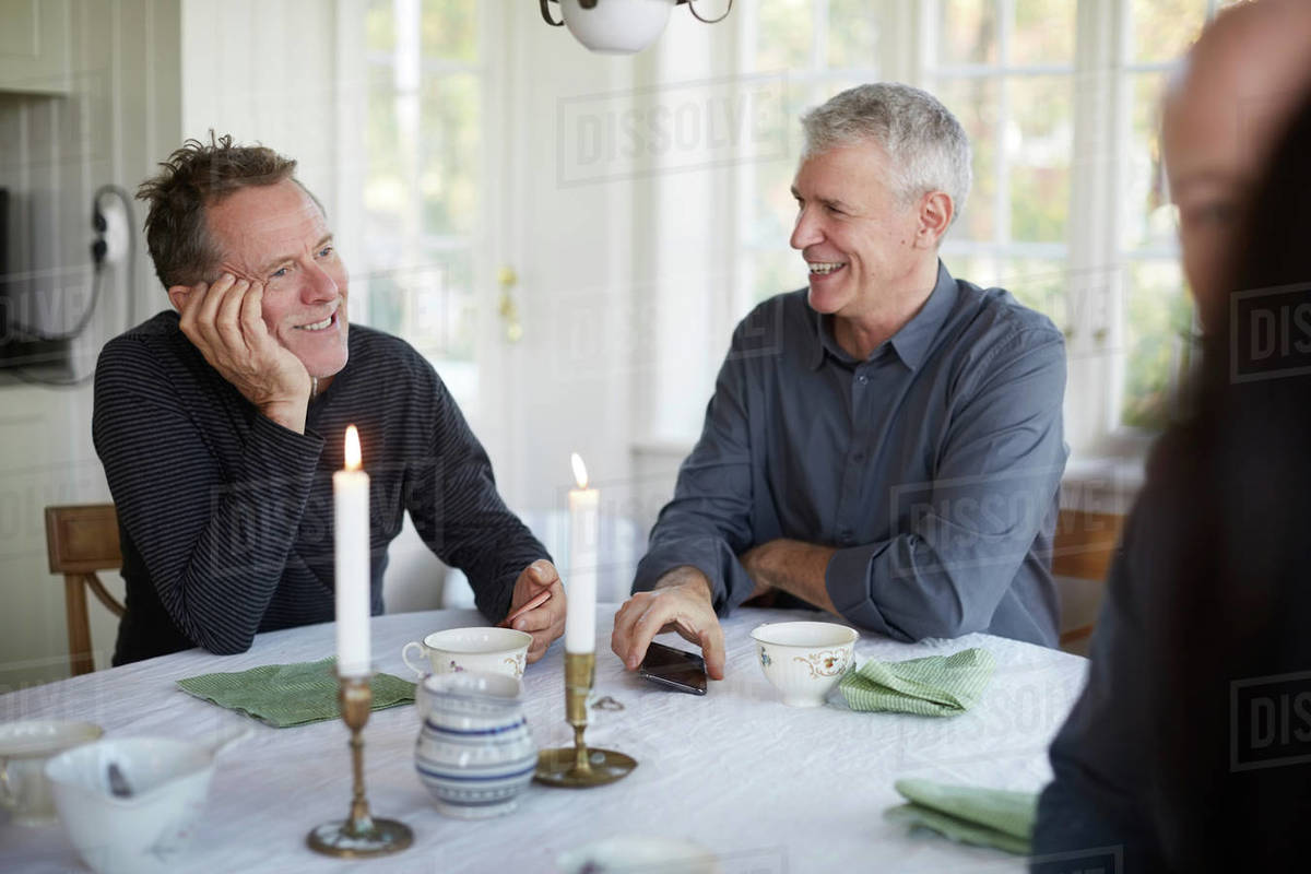 Cheerful mature men talking while sitting at dining table - Royalty ...