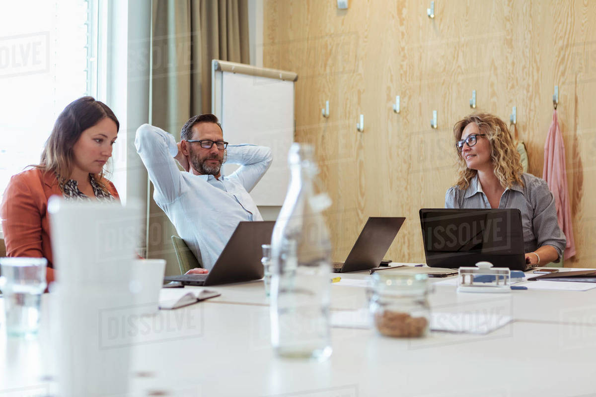 Business colleagues using laptops while sitting at conference table in ...