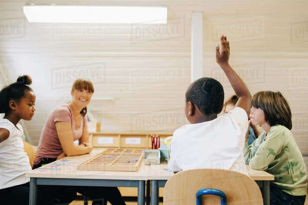 Teacher looking at boy raising hand while answering in classroom ...