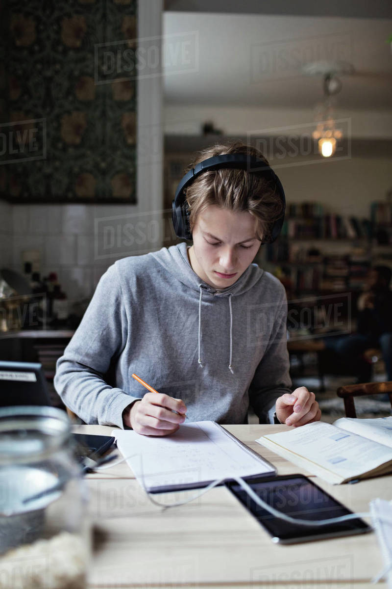 Studious teenage boy listening music while studying on table at home ...