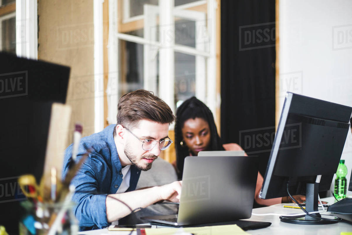 Young computer expert coding in laptop while working with female ...