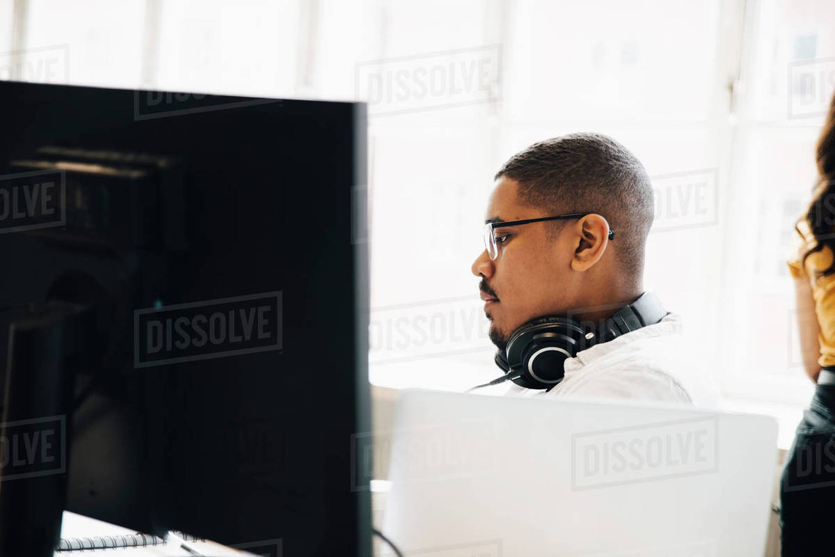 Side view of computer programmer with headphones sitting against window ...
