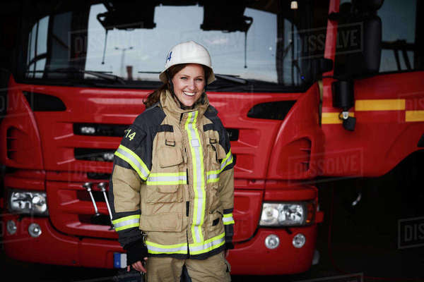Portrait of smiling female firefighter standing in front of fire engine ...