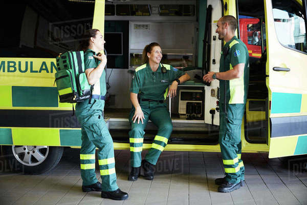 Female paramedic sitting in ambulance while talking with coworkers in ...