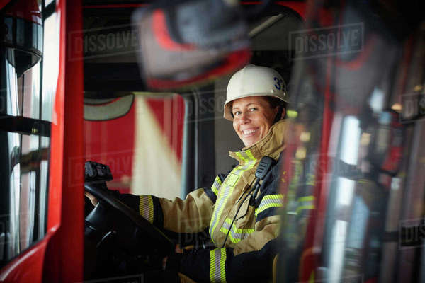 Portrait of smiling female firefighter sitting in fire truck at fire ...