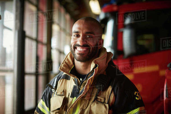 Portrait of smiling male firefighter in uniform at fire station ...