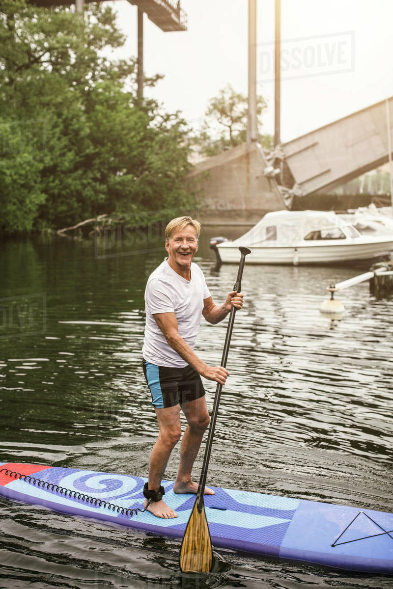 Portrait of smiling senior man paddleboarding in sea during SUP course ...