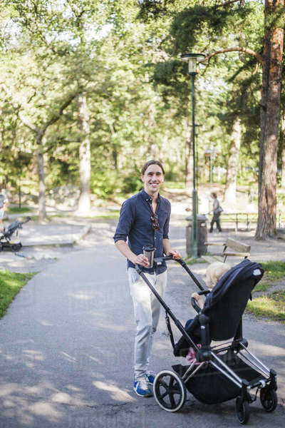 Full length portrait of smiling man standing with son on baby stroller ...