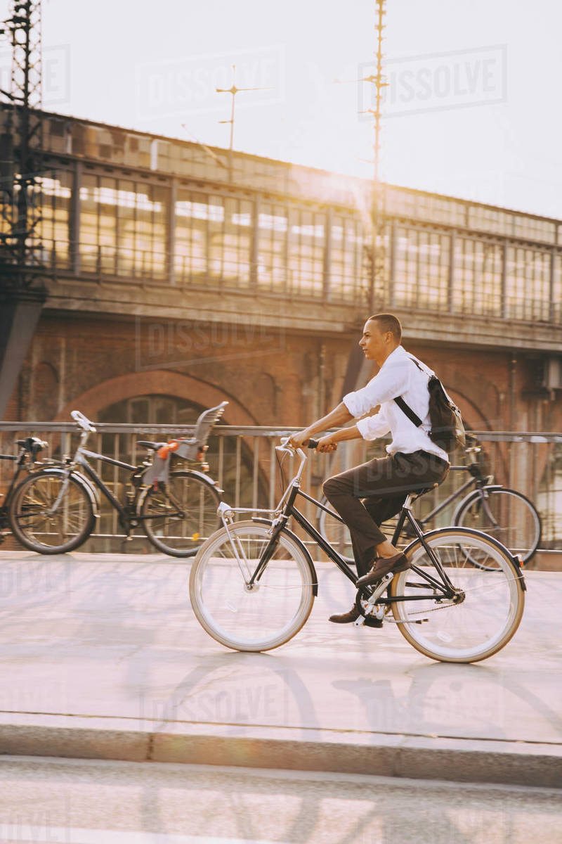 Full length of businessman riding bicycle on street in city against sky ...