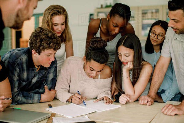 Female studying with friends while professor assisting in classroom ...