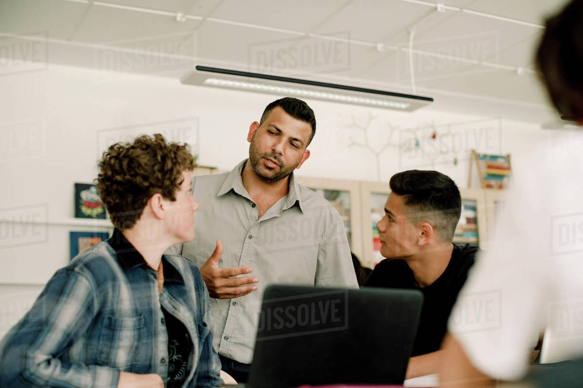 Professor discussing with male students while standing in classroom ...