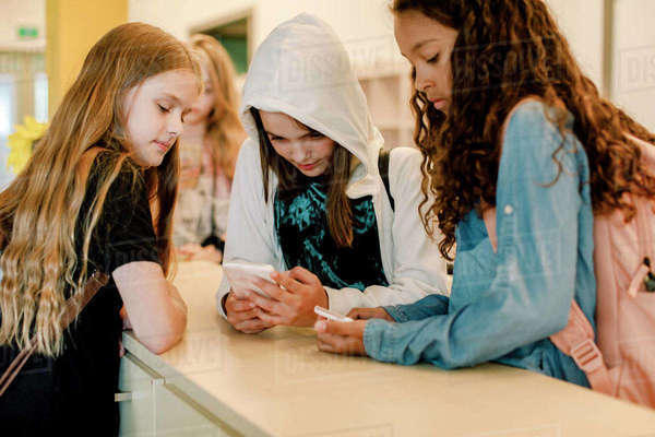 Female students using phone while standing in school corridor during ...