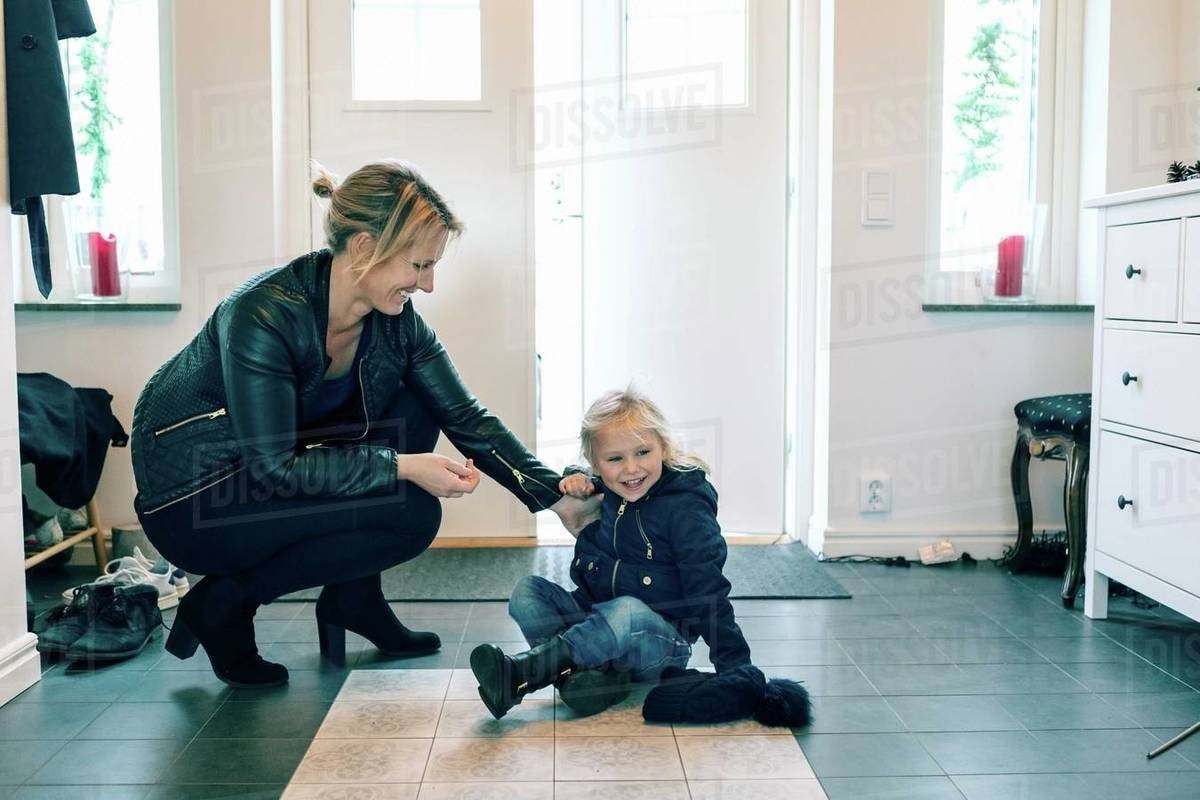 Smiling mother crouching while daughter with knit hat sitting at home ...